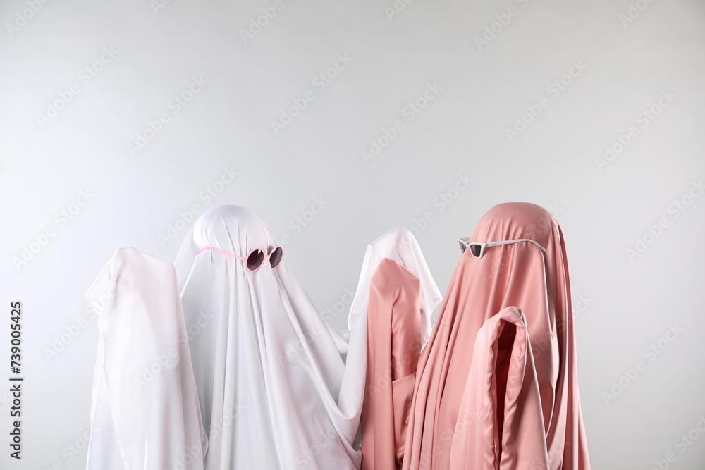Glamorous ghosts. Women in color sheets with sunglasses on light grey ...