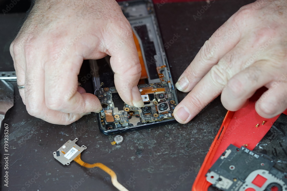 technician repairing mobile phone with his hands, disassembling different types of parts of the ...