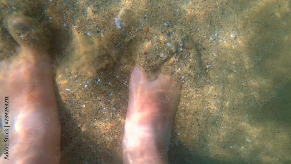 View of a woman's feet digging her toes into the sand under the water ...