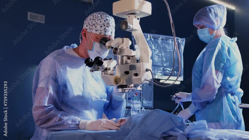 A surgeon looks through a microscope at a patient's eyes in the ...