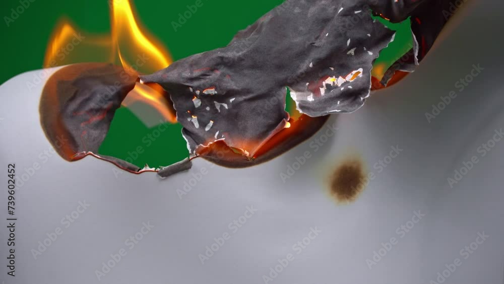 White paper burns from above on a green background copy space. The ...