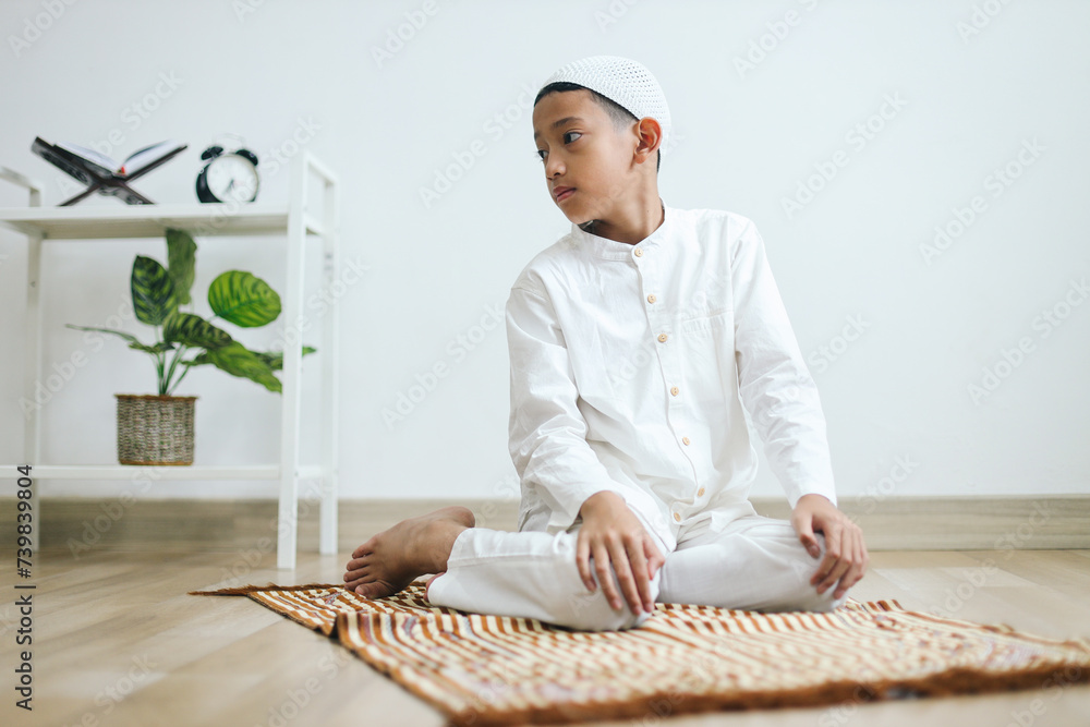 Muslim kid wearing skullcap praying salat in sitting position, reciting ...