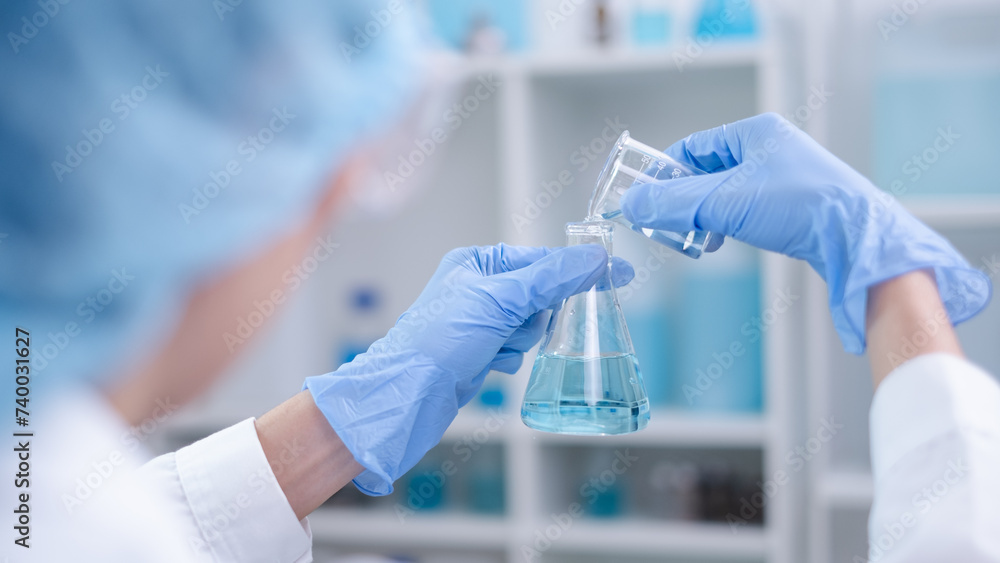 Close-up hands holding pouring blue fluid liquid beaker flask test tube ...