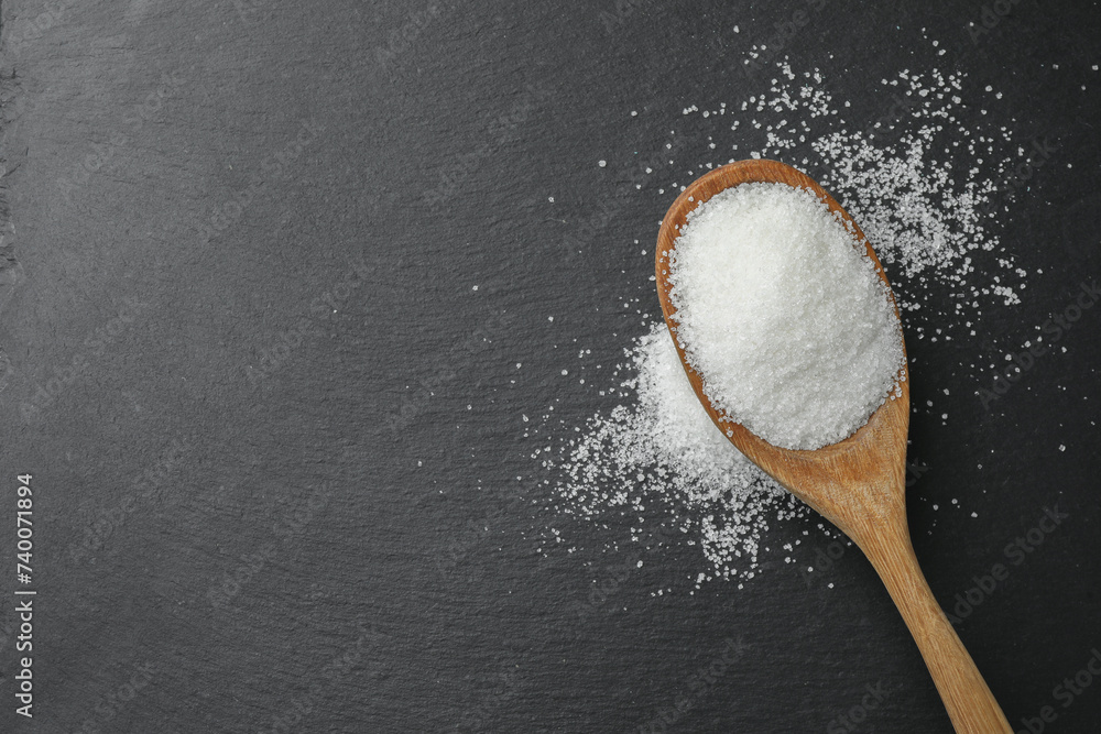 Spoon with granulated sugar on black table, top view. Space for text ...