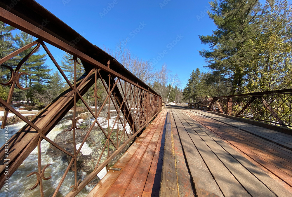 Rusted metal bridge over the river and waterfalls. Elevated footbridge ...