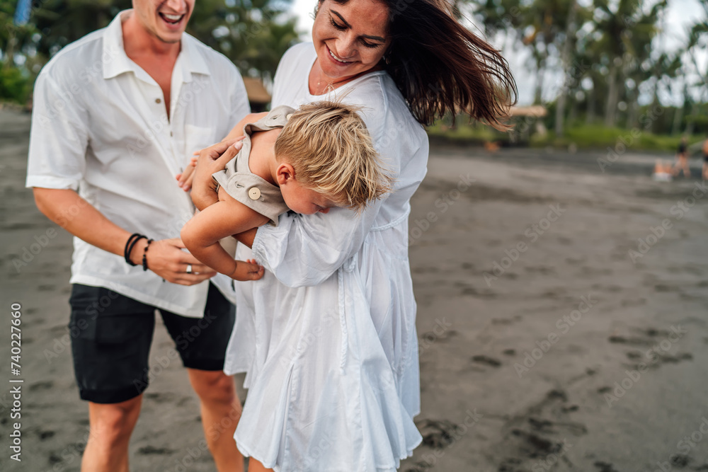 Exuberant young Caucasian family playing on beach; mother lifting ...