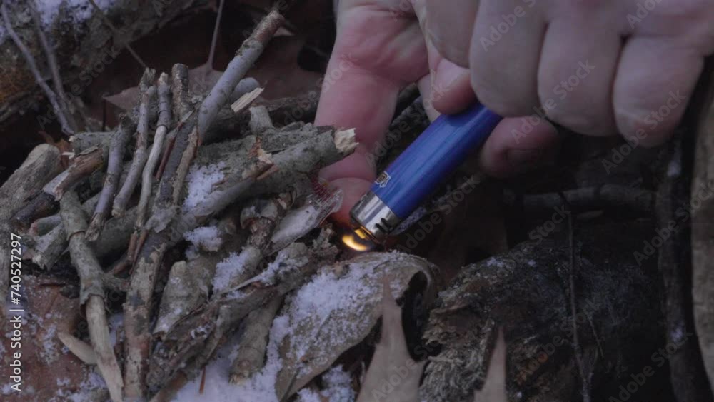 close up as a man uses a bic lighter to ignite dried leaves and small ...