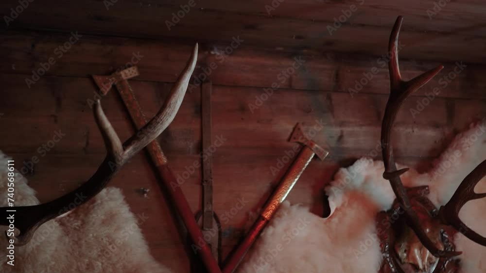 Deer antlers hang on the wall with an ax and other metal weapons in the ...