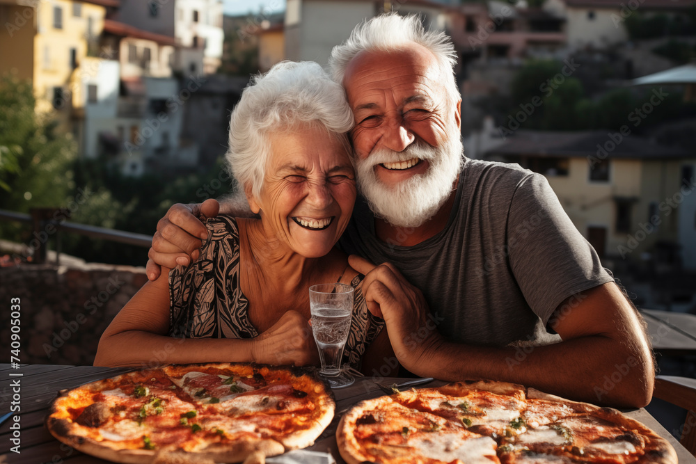 Happy senior old couple have fun eating a pizza together outdoor in traditional italian pizzeria ...