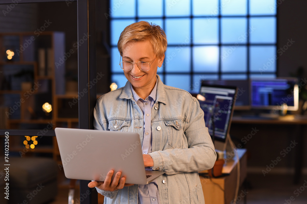 Mature female programmer working with laptop in office at night Stock ...