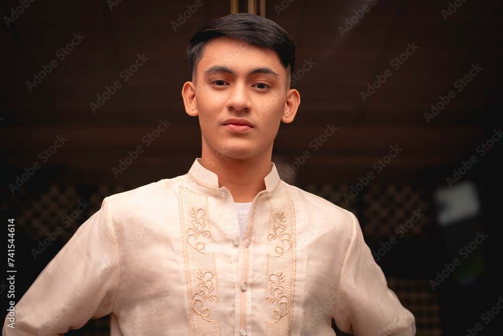 A young FIlipino man wearing a traditional Barong Tagalog shirt, inside ...