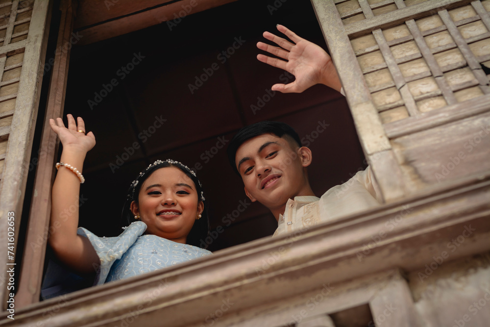 A joyful young Filipino couple dressed in traditional clothing waving ...
