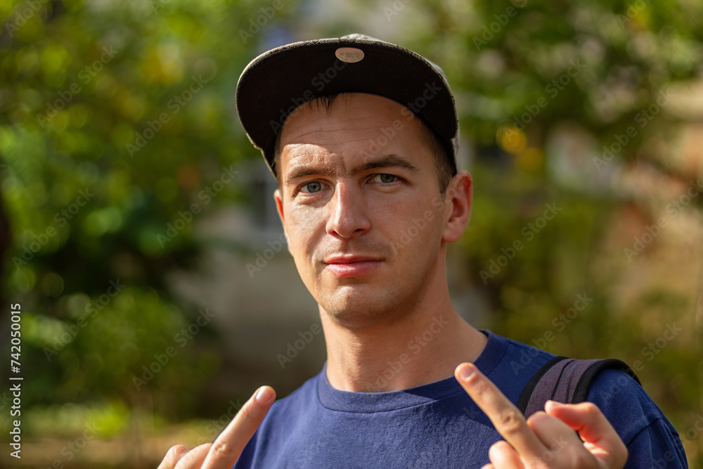Obscene gesture. Young man in baseball cap and T-shirt shows the middle ...