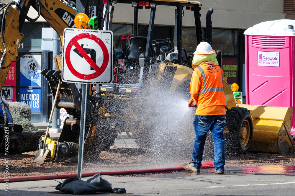 A construction worker, clad in a white hard hat and orange safety vest ...