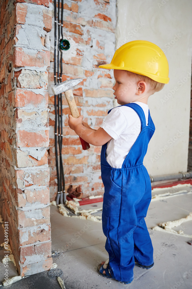 Full length of child construction worker standing by brick wall and ...