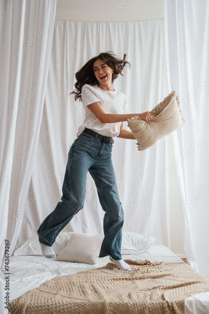 Jumping with pillow. Young beautiful woman is at home on the bed Stock ...