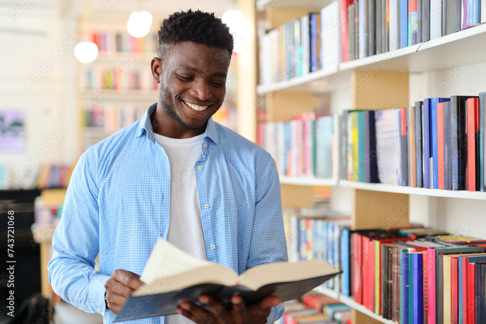 A young man stands confidently in a library, surrounded by shelves of ...