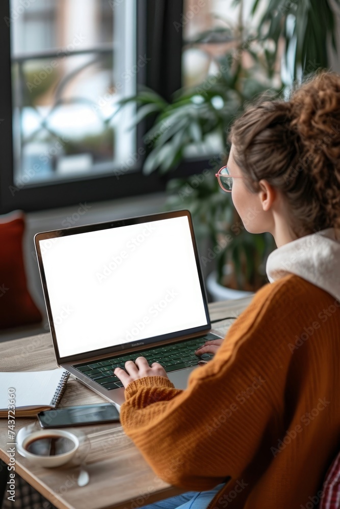 Over shoulder view of woman student elearning looking at white mock up blank screen using laptop ...
