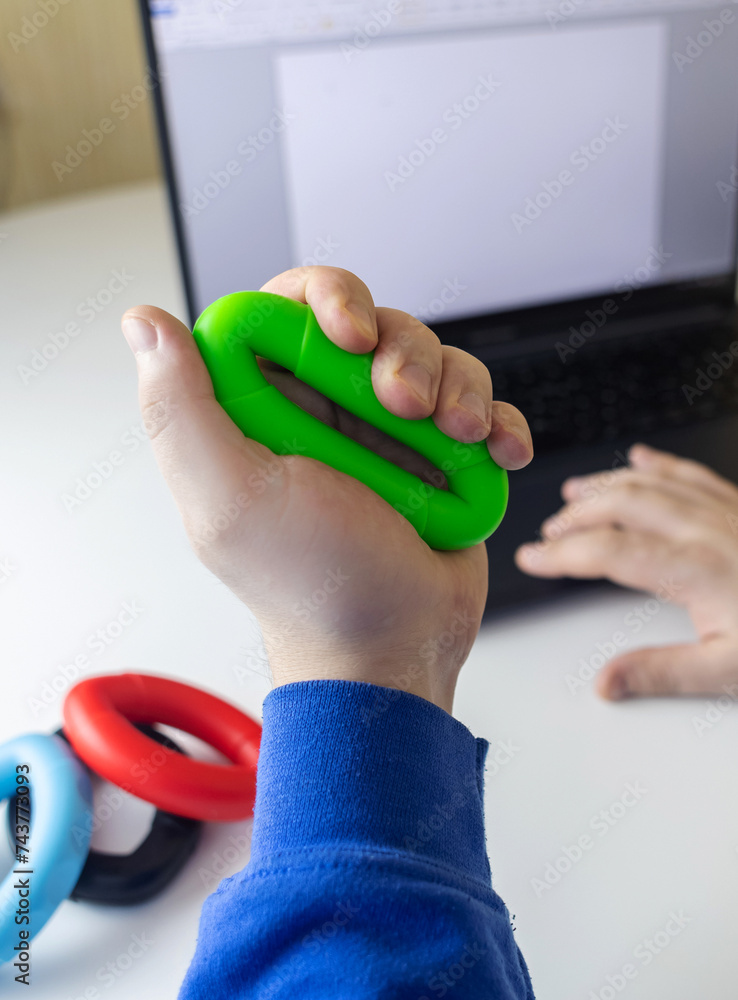 Hand gripper. Man squeezes rubber expander while working on his laptop ...