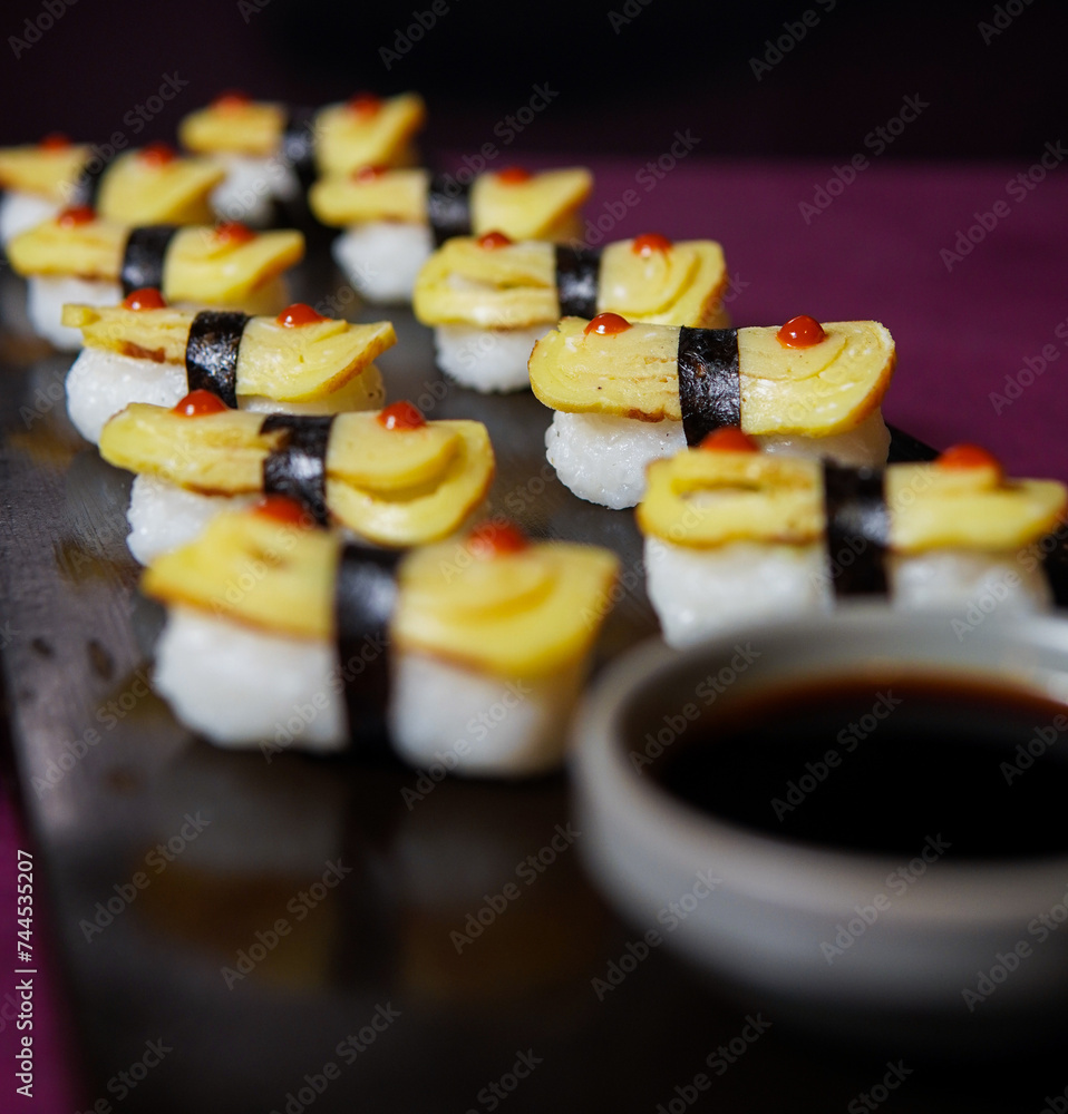 Tamago Nigiri served on a black wooden plate, avocado, cucumber, lump ...