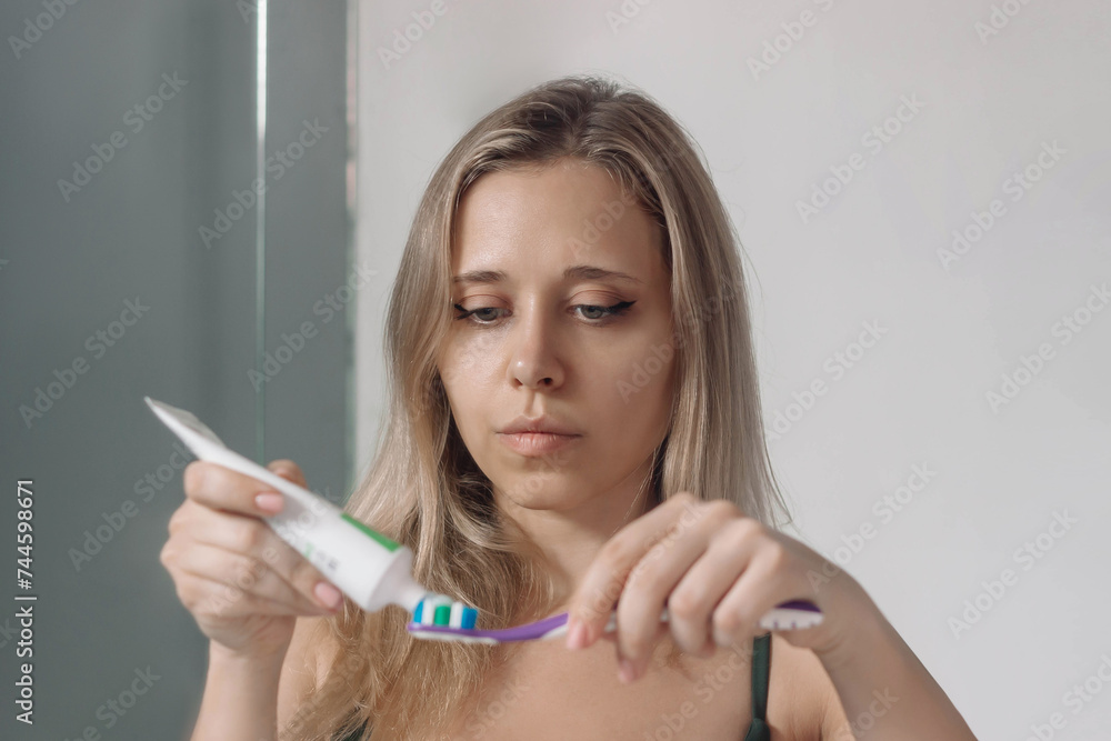 A young attractive caucasian blonde woman squeezing toothpaste from a ...