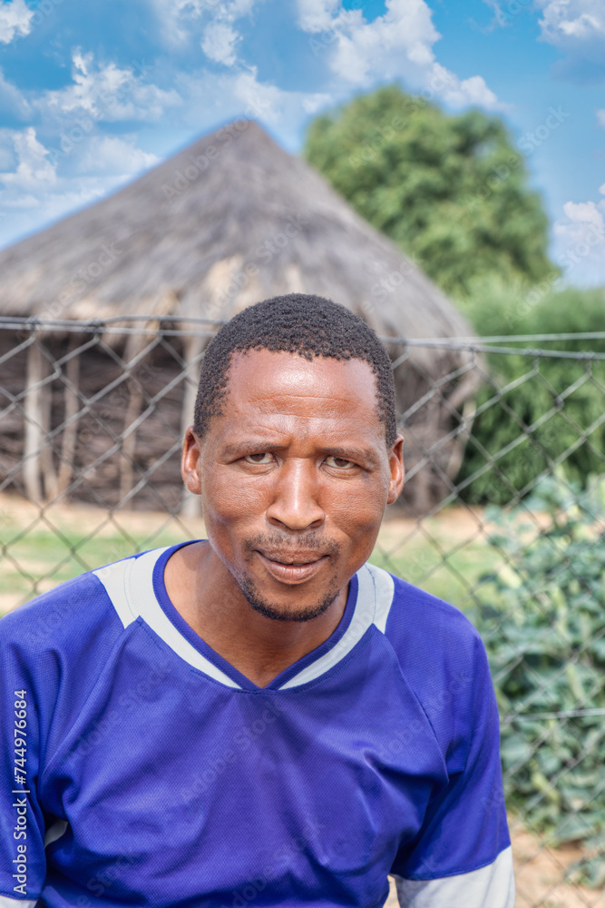 village african man in the yard, in the background hut with thatched roof and blue sky , south ...