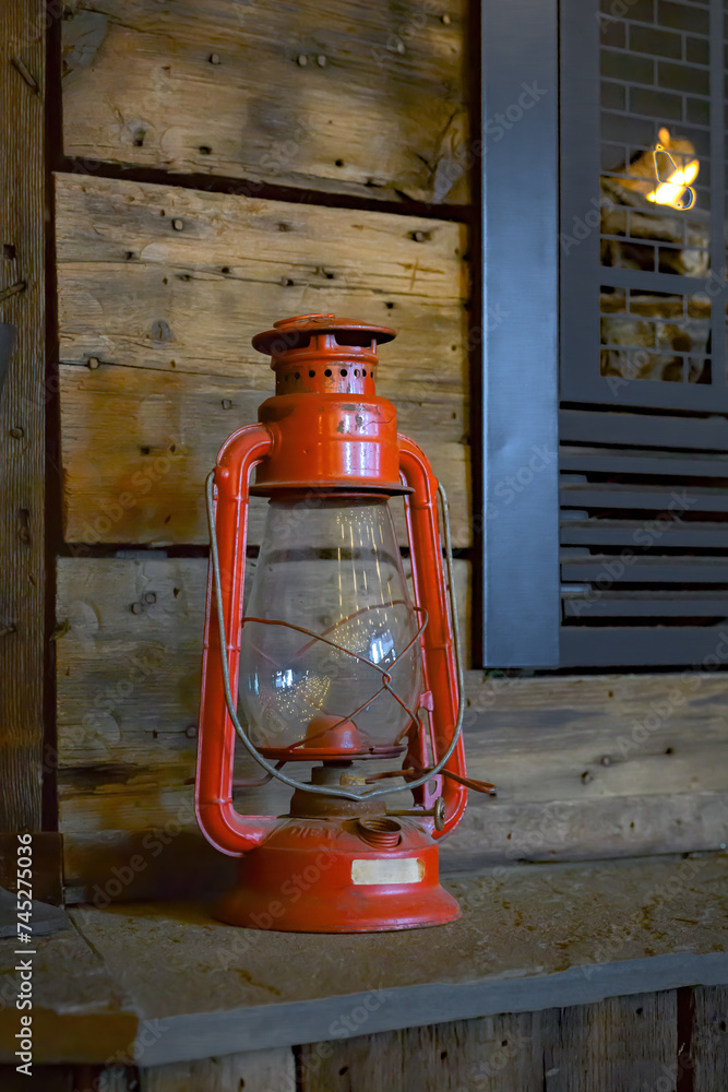 An old vintage red hurricane lamp sits on the wooden ledge beneath the ...