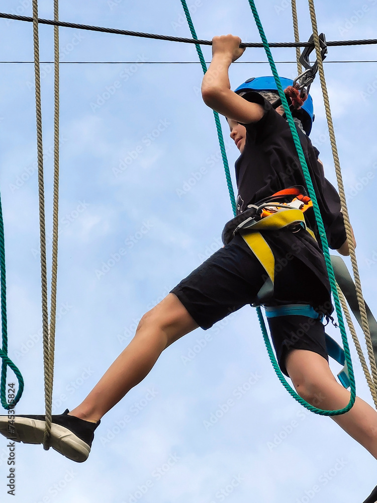 A teenage boy walks on a rope suspension bridge in a rope amusement ...