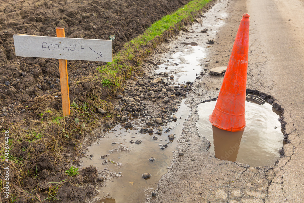 Pothole, deep pothole filled with rainwater, with traffic cone and sign ...