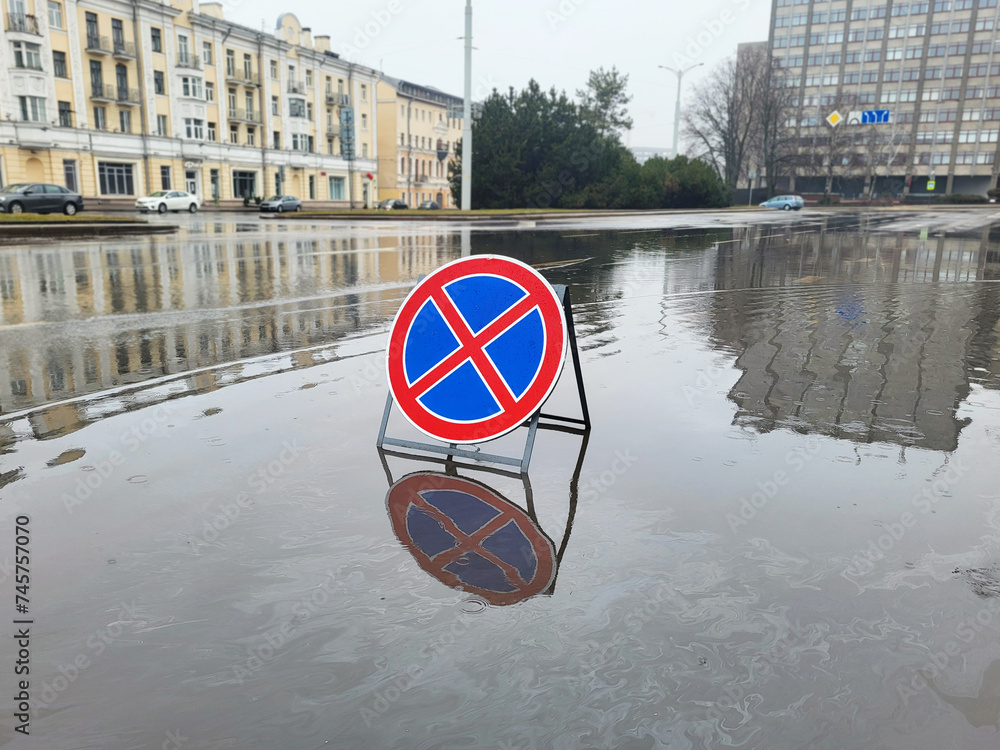 No parking, no waiting traffic sign stands in the deep puddle. Round ...