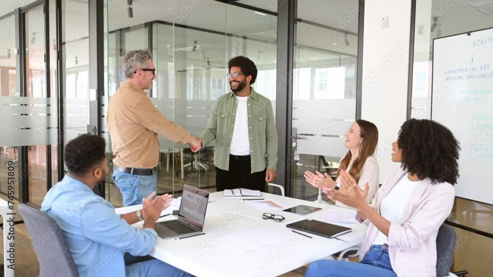 A team circles around a meeting table where a handshake between two ...