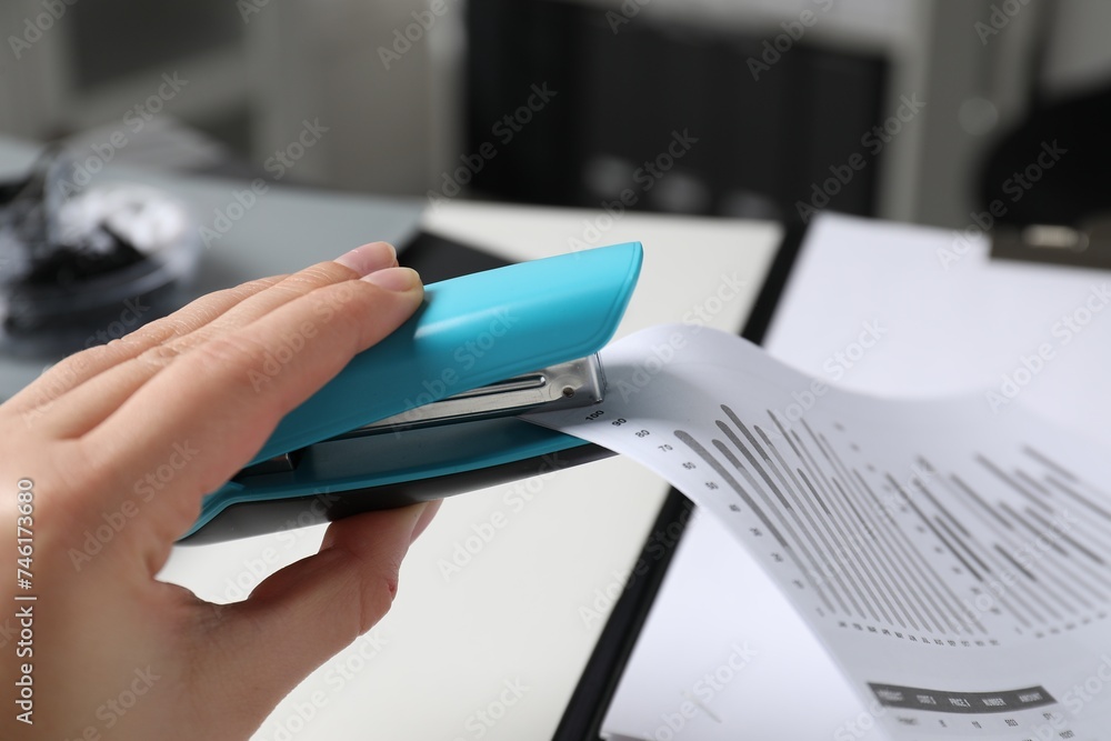 Woman with documents using stapler at white table indoors, closeup ...