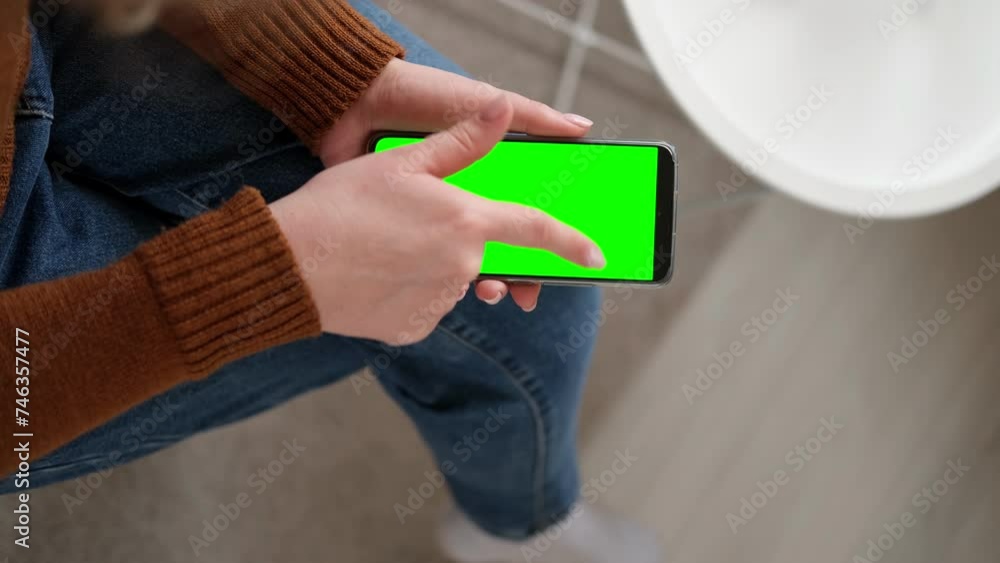 Young woman sitting at home holding smartphone green mock-up screen in ...
