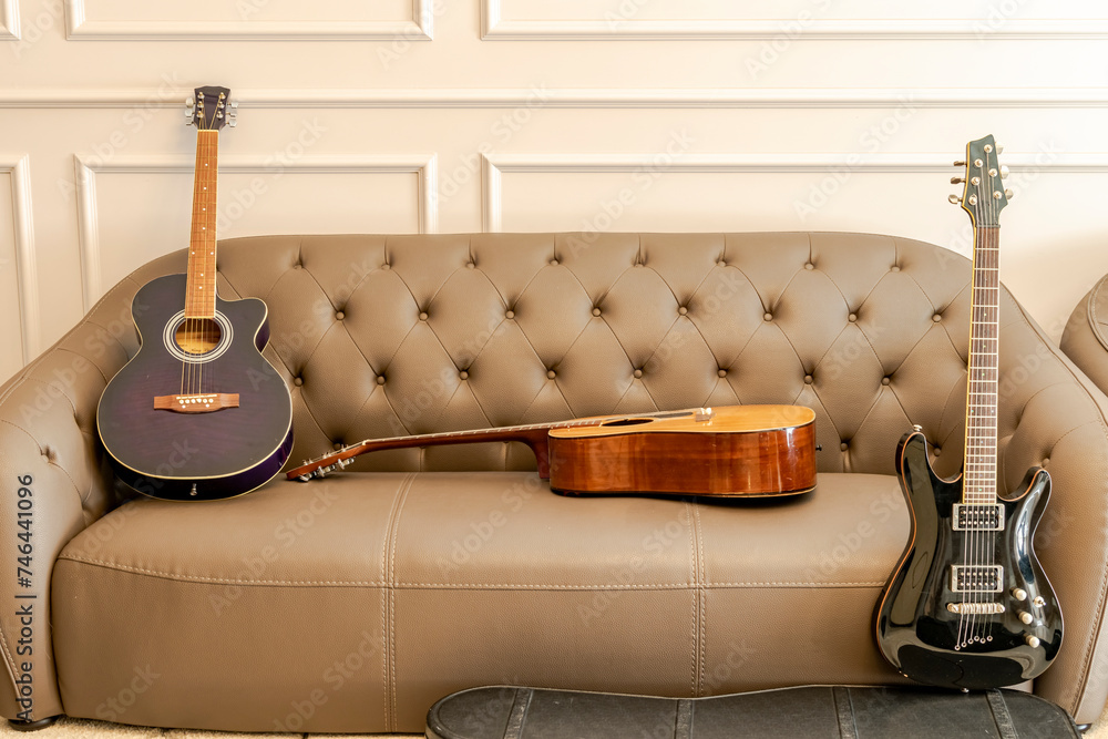 Three guitars set on a brown leather sofa in the living room. A black ...