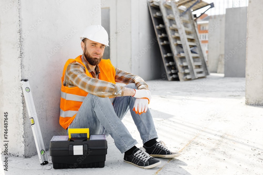 Builder repairman, foreman in safety helmet and vest sitting down to ...