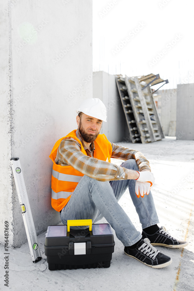 Builder repairman, foreman in safety helmet and vest sitting down to ...