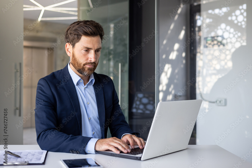 Concentrated young male office worker sits at a desk in a suit and ...