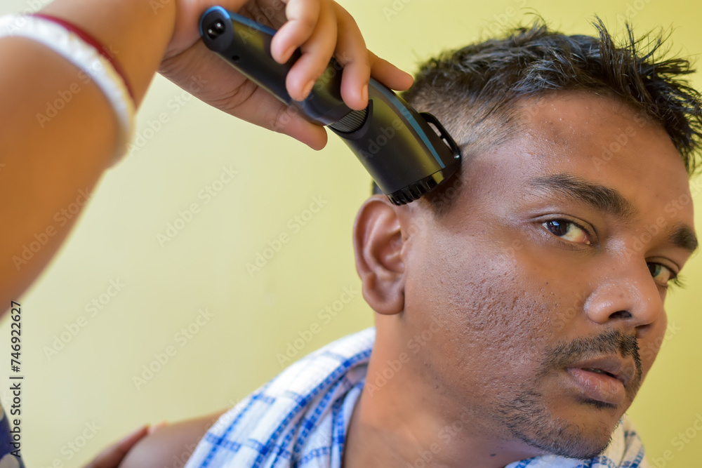 Happy young Indian man being trimmed with an electric clipper machine ...