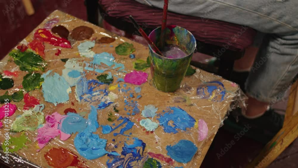 Artist's hand mixing paint colors on a palette covered in vibrant ...