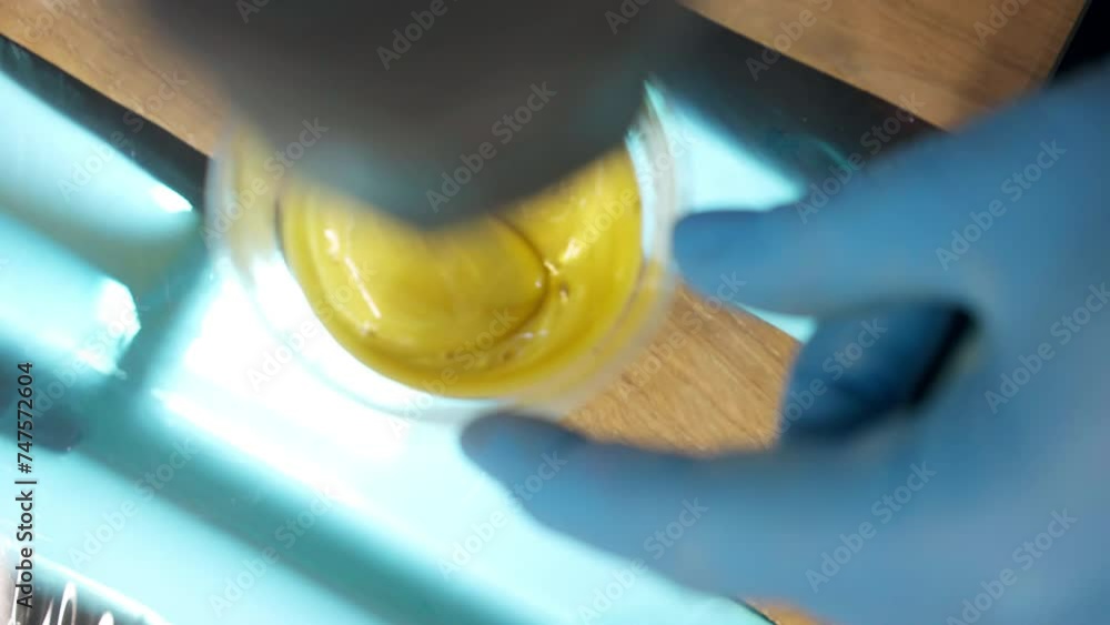 Dense yellow solution mixing in plastic cup with small industrial mixer ...