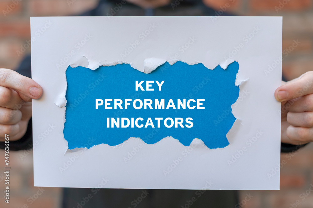Man holding white and blue sheets of paper with text: KEY PERFORMANCE ...
