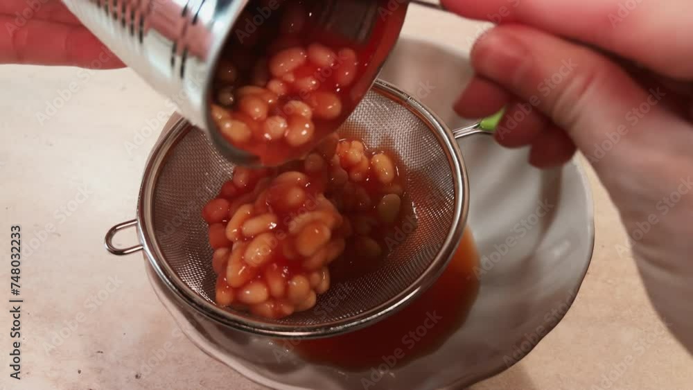 POV pouring beans cooked in tomato sauce into collander. Cullender with ...