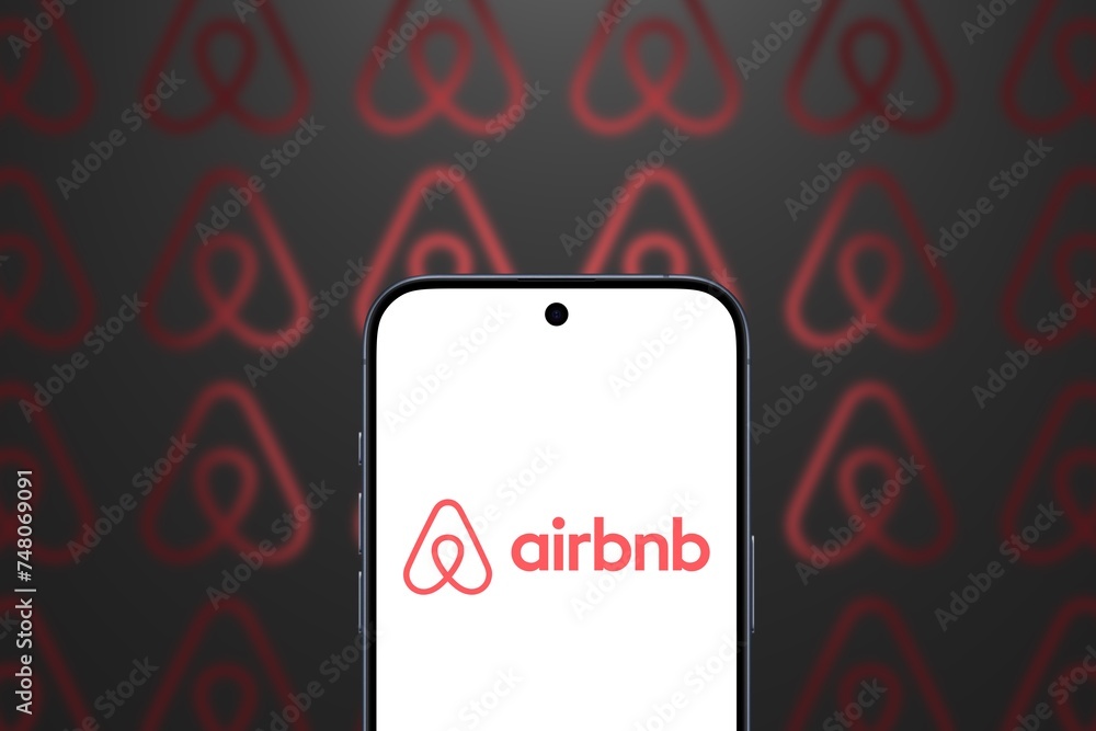airbnb Logo is displayed on a modern smartphone, many blurred pink Airbnb Logos in front of a ...
