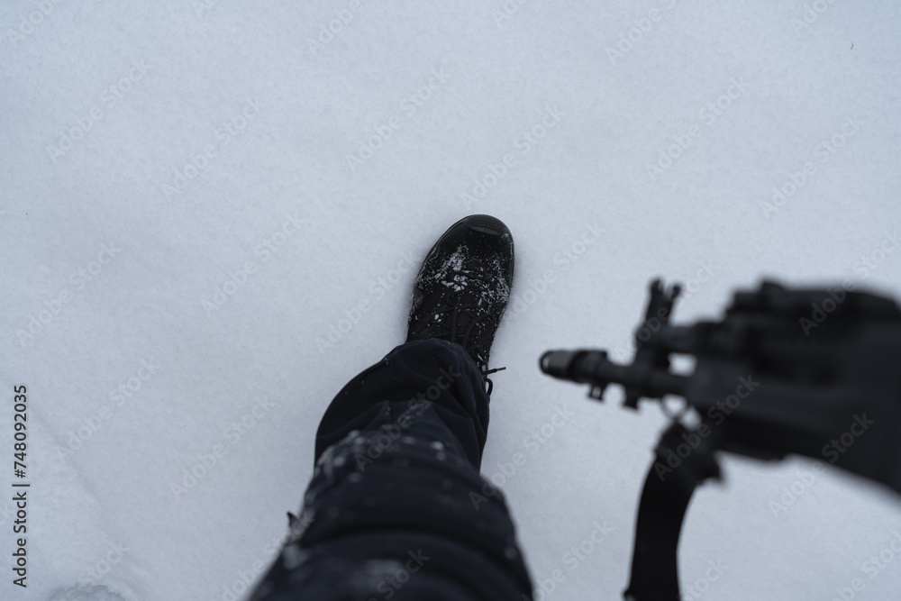 The foot of a soldier in a tactical boot and with a rifle against the ...