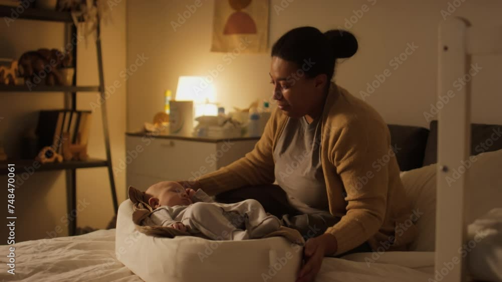 Full shot of young African American or Hispanic mother sitting on bed ...