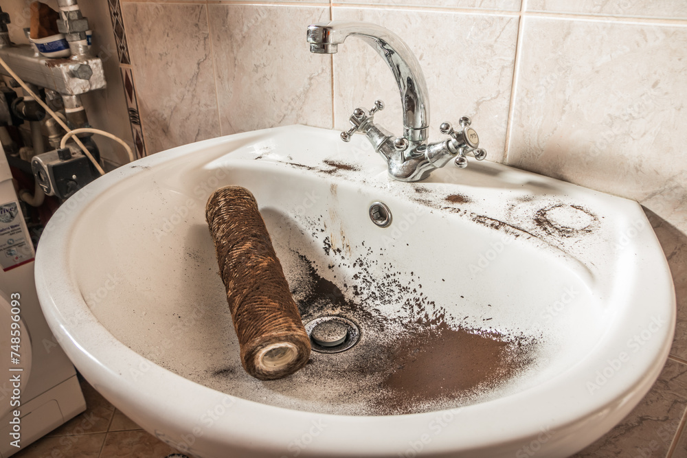Falling dirty particles from a water filter in a white washbasin ...