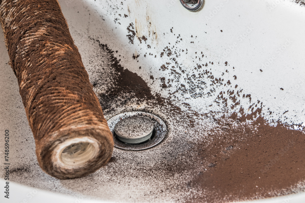 Falling dirty particles from a water filter in a white washbasin ...