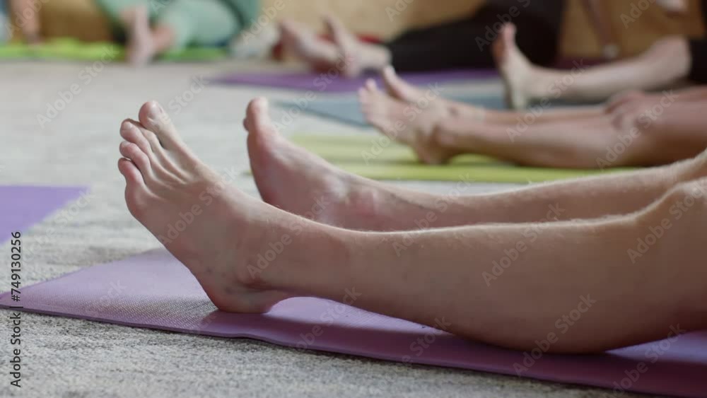 Legs of women sitting on mat doing warming exercises during yoga ...
