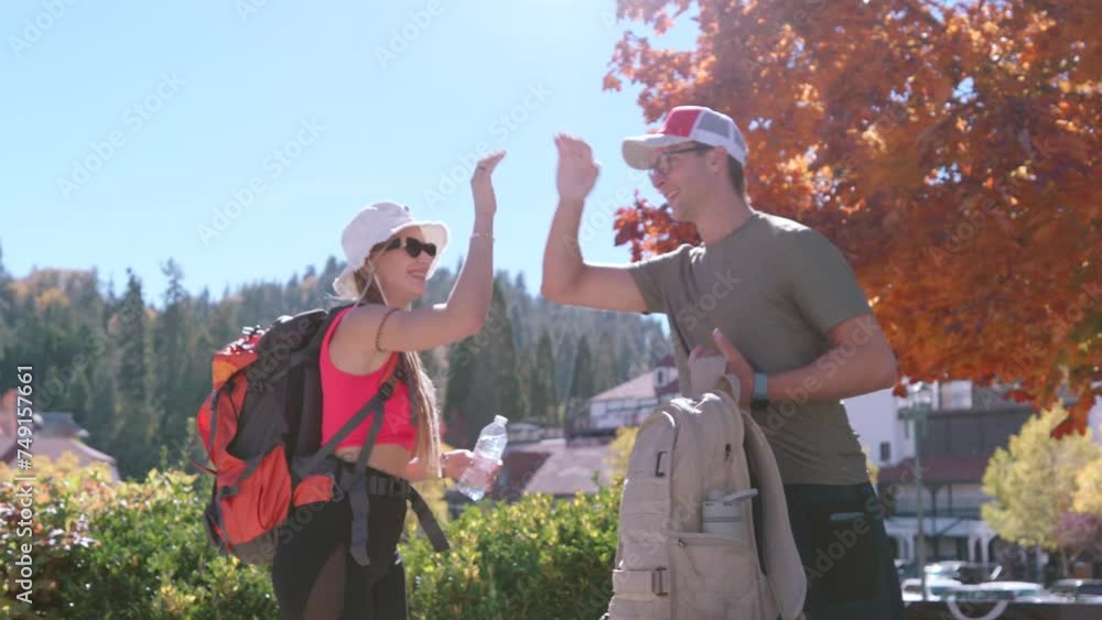 Cheerful hikers high-five in a sunny mountain town with autumn leaves ...