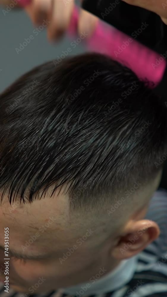 A barber man with a tattoo on his arm makes a haircut to a brunette guy ...